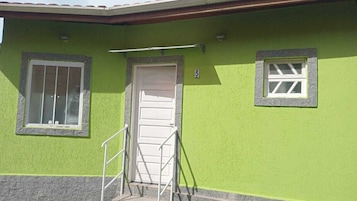 Um edifício com fachada verde, porta branca e duas janelas com molduras brancas.