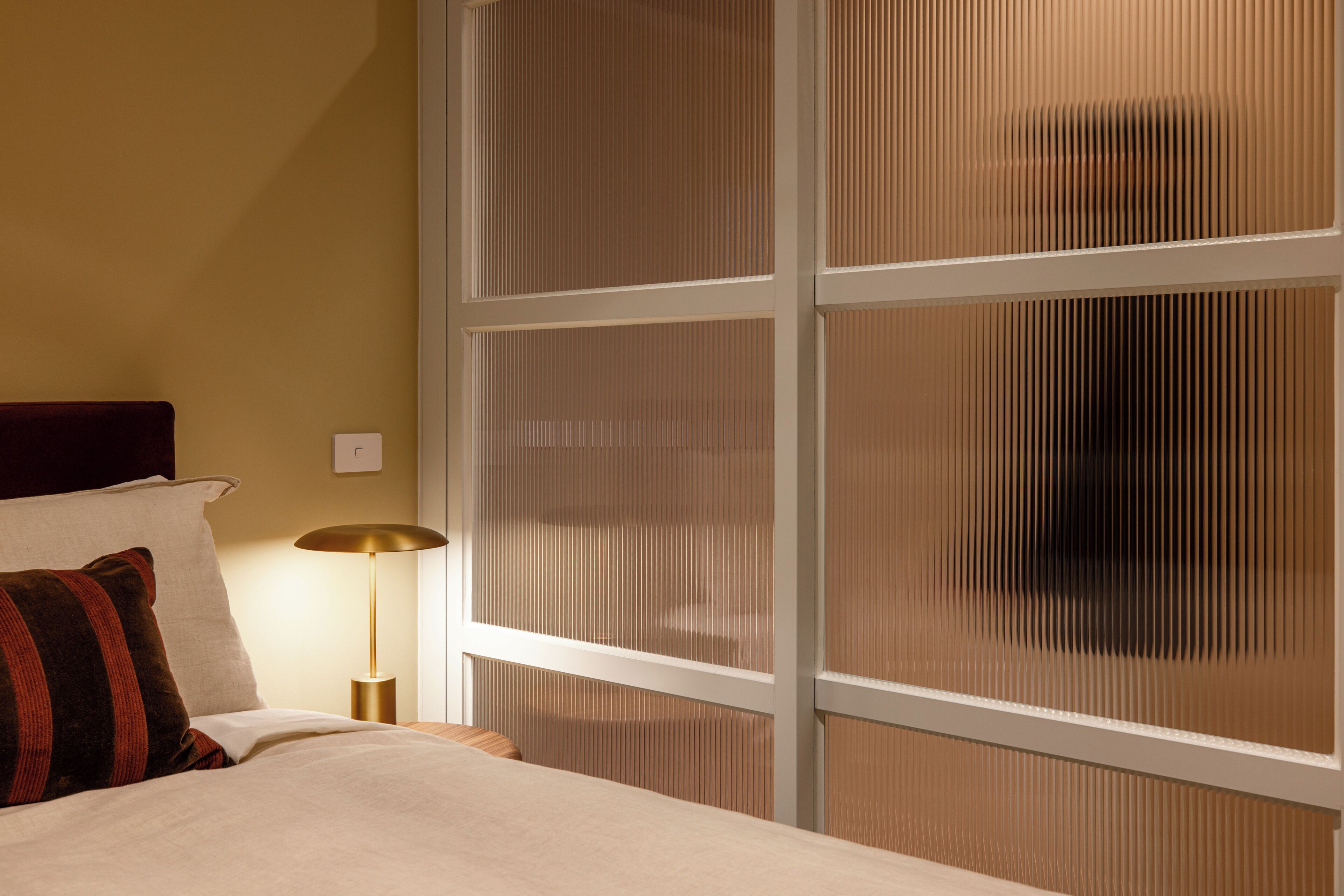 Quarto de hotel com cama, mesa de cabeceira, luminária e janela com persianas.