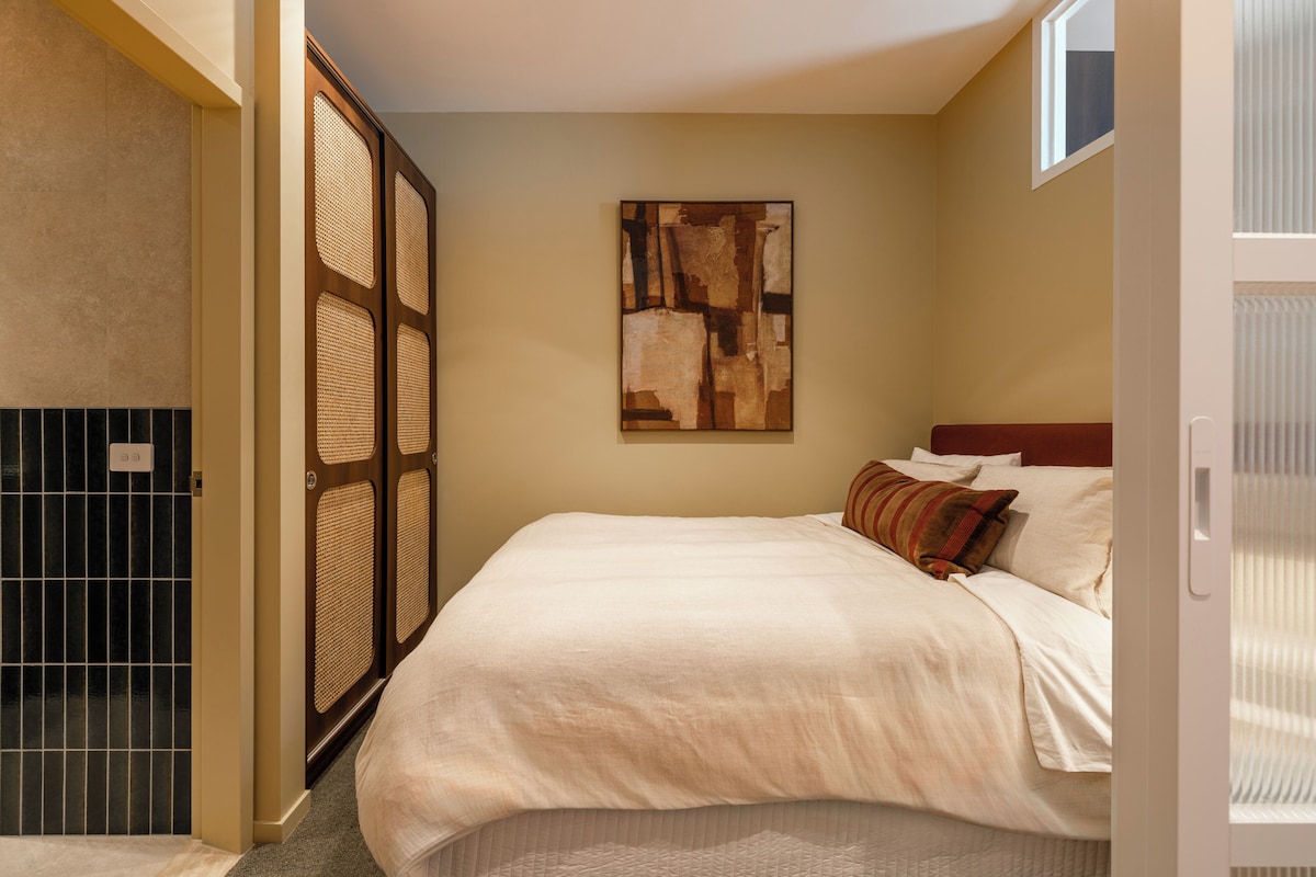 Quarto de hotel com uma cama, uma porta com desenho trançado e um quadro na parede.
