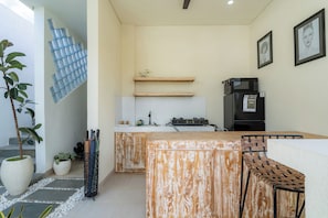 Cozinha equipada com micro-ondas, fogão e frigorífico. Há estantes de madeira acima do balcão e uma planta à esquerda.