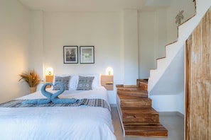 Quarto com cama, duas imagens emolduradas, abajures, escada de madeira e um objeto decorativo fixado na parede.