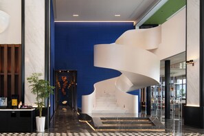 Um lobby moderno com escadaria em espiral, piso de mármore e padrão de ladrilho quadriculado.