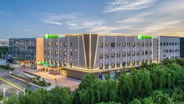 Um hotel Holiday Inn Express com design moderno, apresentando uma ampla área de estacionamento e um jardim bem cuidado.