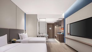 Quarto de hotel com duas camas, televisão, espelho, banheiro e uma pequena cozinha.