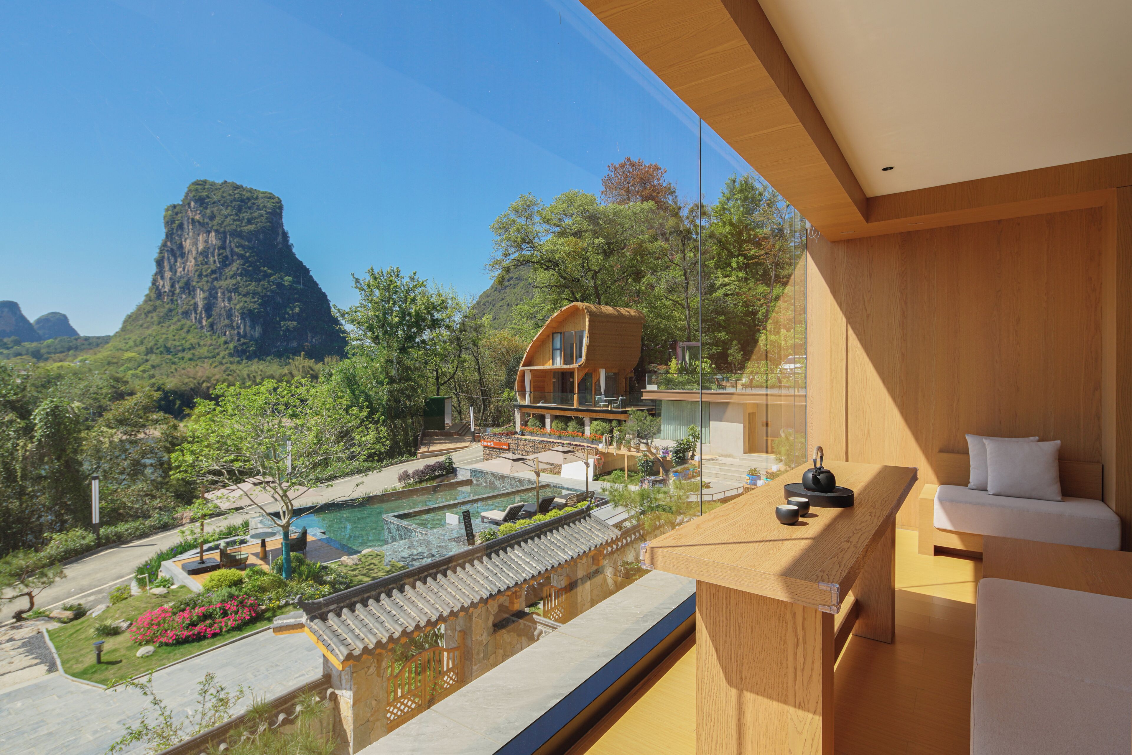 Quarto de hotel moderno com varanda e vista para uma piscina e vegetação exuberante.