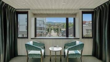 Quarto com duas cadeiras, uma mesa pequena e vista para a cidade através de grandes janelas.