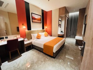 Quarto de hotel com cama, escrivaninha, cadeira e um quadro na parede.
