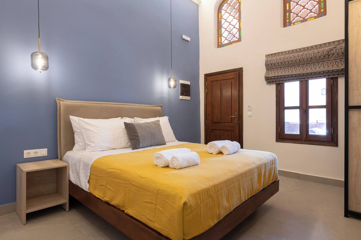 Quarto com cama, mesa de cabeceira e janela com vista.