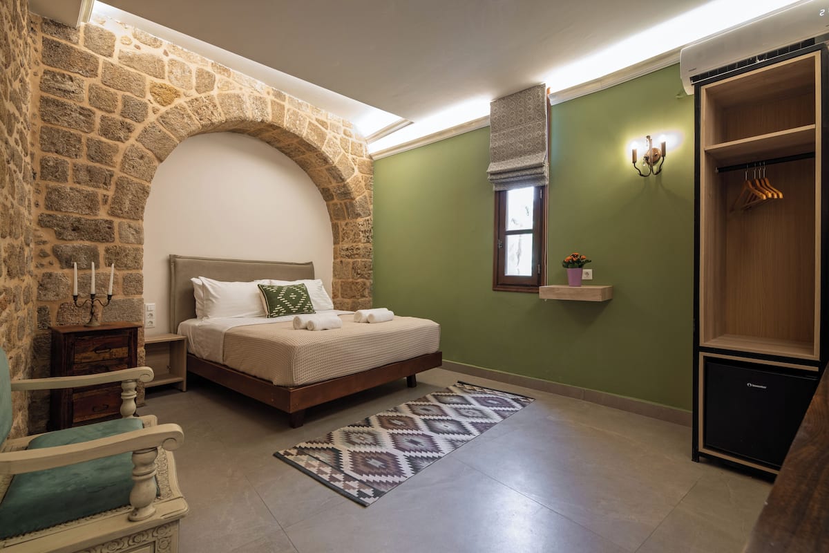 Quarto com arco de pedra, cama, mesa de cabeceira, cômoda e janela com vista.
