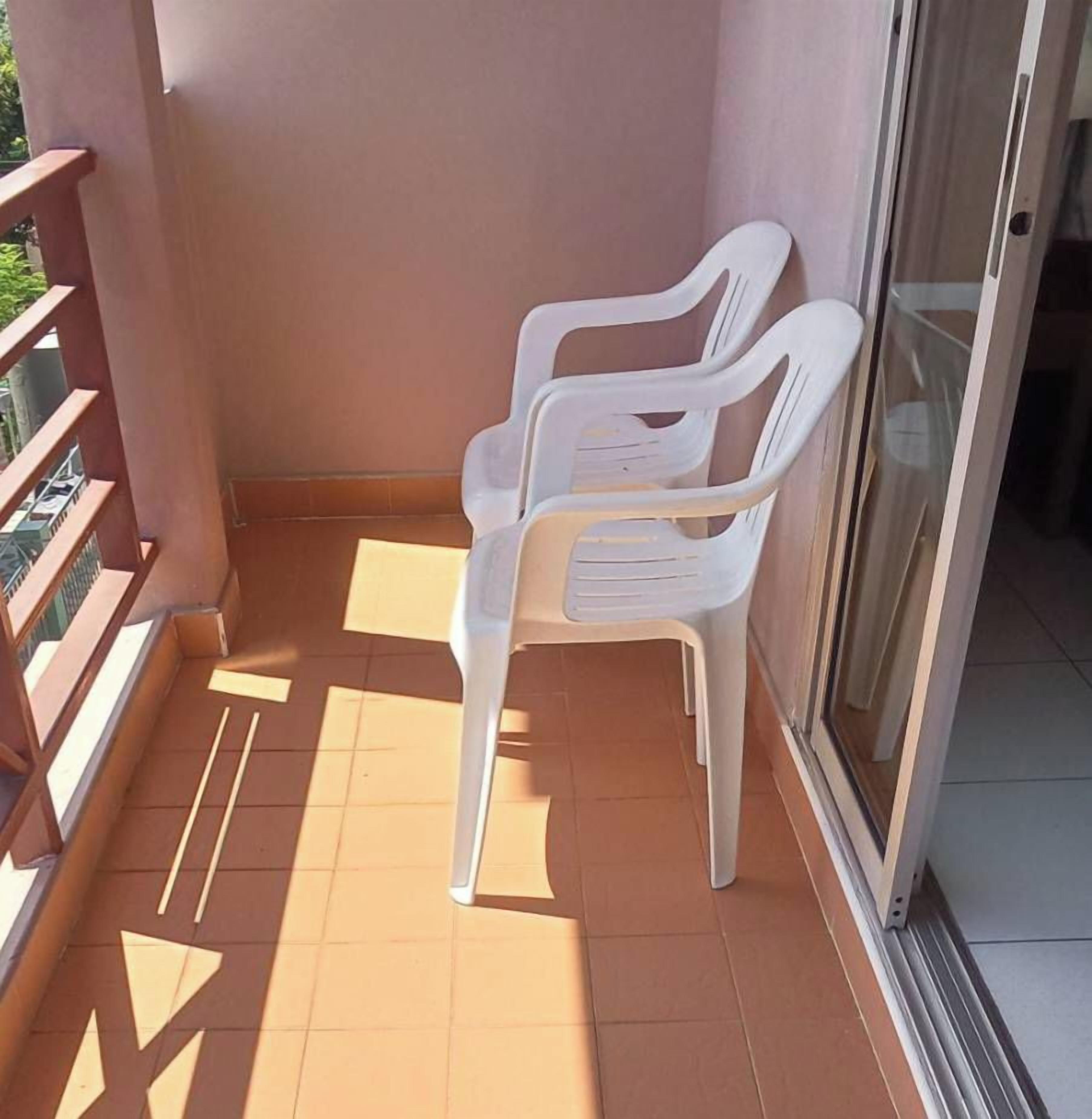 Varanda com duas cadeiras de plástico branco e uma porta de correr de vidro.