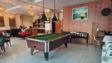 Uma sala de jogos com mesa de bilhar, cadeiras e alvo de dardos.