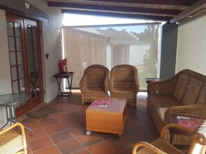 Uma varanda coberta com móveis de vime, uma mesa pequena e uma porta que dá para o exterior.