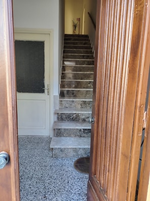 Uma escadaria com corrimão, uma porta com painel de vidro jateado e piso salpicado.