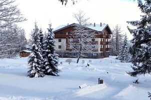 Um edifício com vários andares e telhado inclinado, rodeado por árvores cobertas de neve e solo coberto de neve.