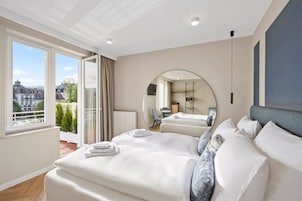 Quarto de hotel com uma cama grande, varanda com vista, espelho redondo e escrivaninha com cadeira.