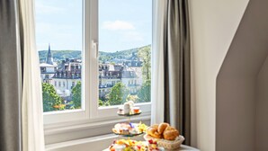 Uma mesa de café da manhã com doces, frutas e vista para uma cidade pela janela.