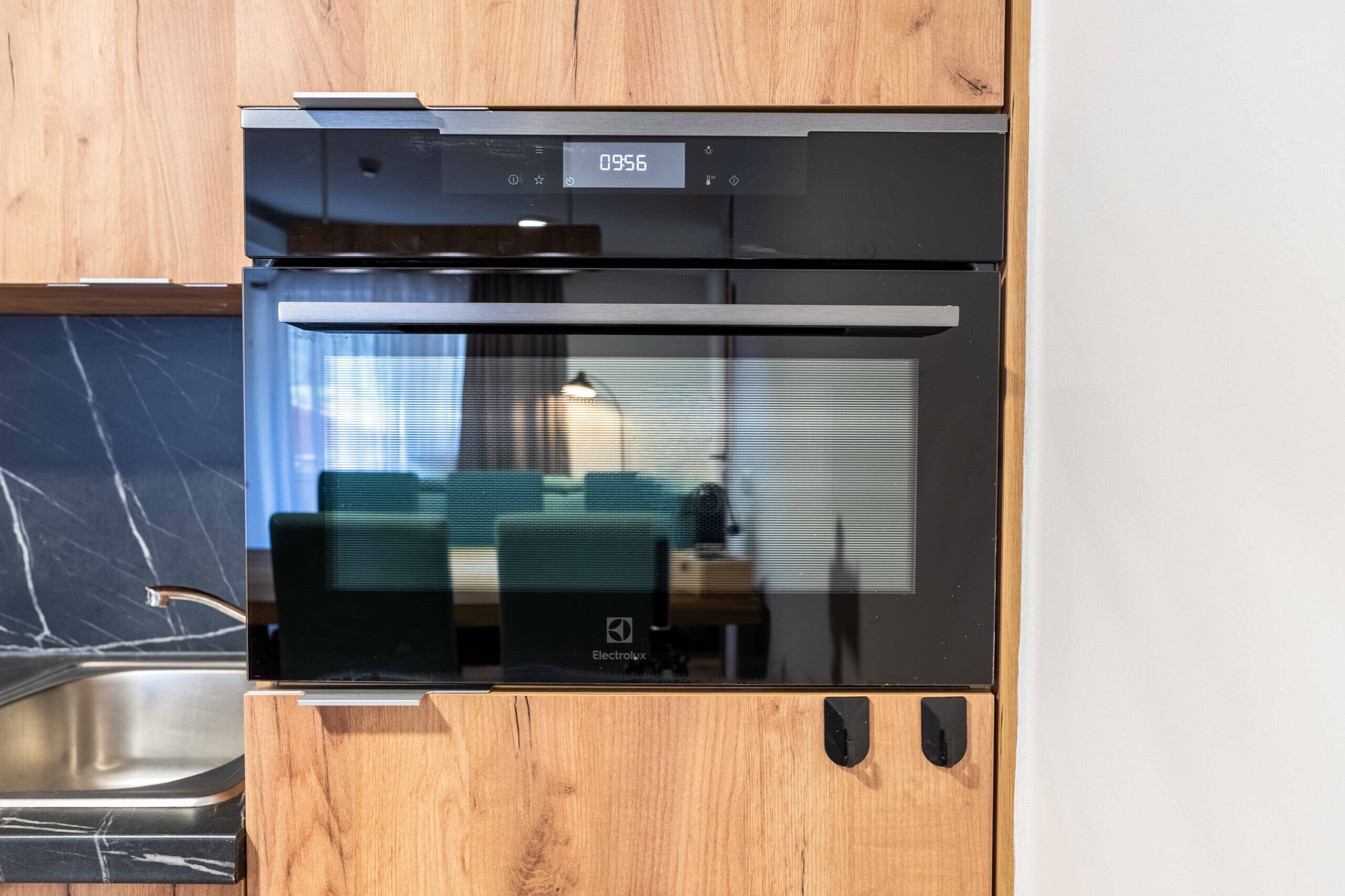 Uma cozinha moderna com forno embutido e micro-ondas, pia de aço inoxidável e armários de madeira.