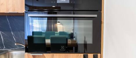 Uma cozinha moderna com forno embutido e micro-ondas, pia de aço inoxidável e armários de madeira.