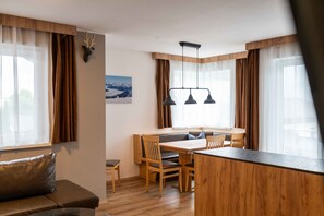 Um quarto com uma mesa de jantar de madeira, cadeiras, um sofá e um chifre de veado fixado na parede.