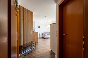 Um corredor com um banco de madeira, um painel de madeira e uma porta que dá para uma sala de estar com um sofá e uma mesa de centro.