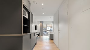Uma cozinha moderna com micro-ondas embutido, piso de madeira e vista para o exterior através de uma porta de vidro.