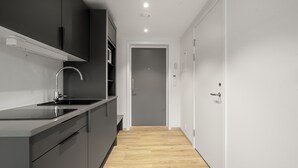 Uma cozinha moderna com armários cinzentos, bancada preta e chão de madeira que leva a uma porta.