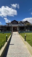 Um edifício com um caminho de pedras que leva a uma porta de madeira, cercado por uma grade de metal e vegetação.