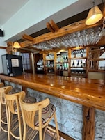 Uma área de bar com vigas de madeira, paredes de pedra e banquetas.