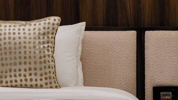 Cama bem arrumada com roupa de cama branca e bege, cabeceira de madeira e luminária fixada na parede.