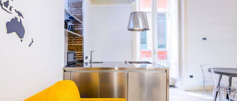 Cozinha moderna com ilha de aço inoxidável, sofá amarelo vibrante e vista desobstruída para o exterior.