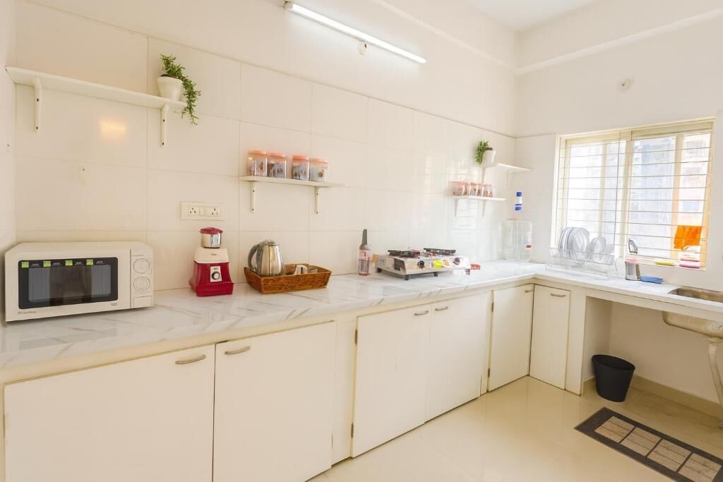 Uma cozinha com armários brancos, micro-ondas, cafeteira e janela com vista.