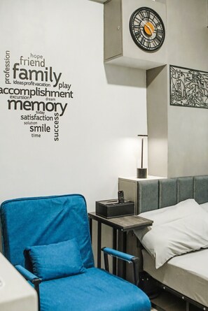 Quarto de hotel com arte de parede em nuvem de palavras, um relógio, uma cama, uma cadeira e uma mesa de cabeceira.