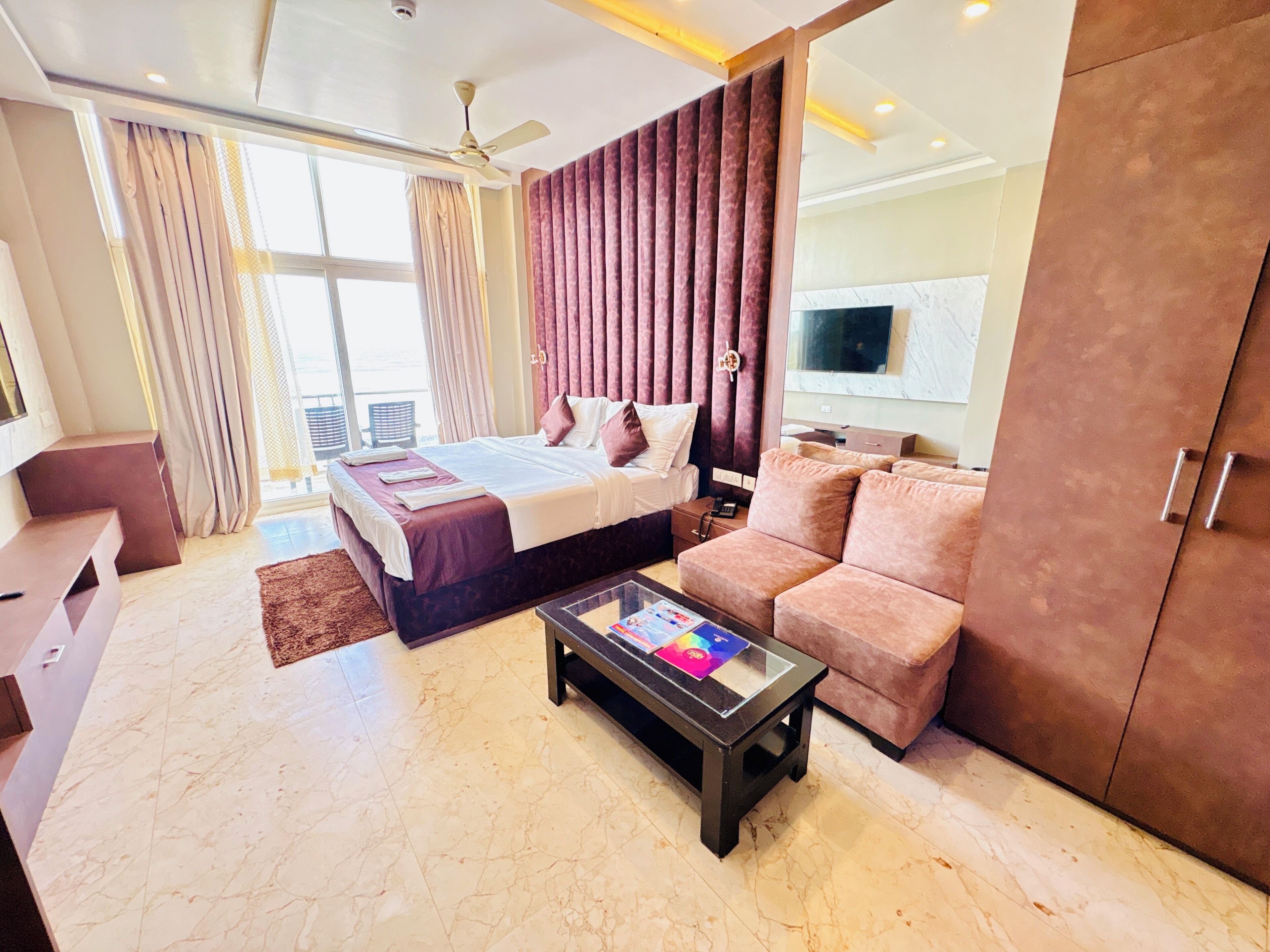 Quarto de hotel moderno com uma cama, um sofá, uma mesa de centro, uma televisão e um guarda-roupa.