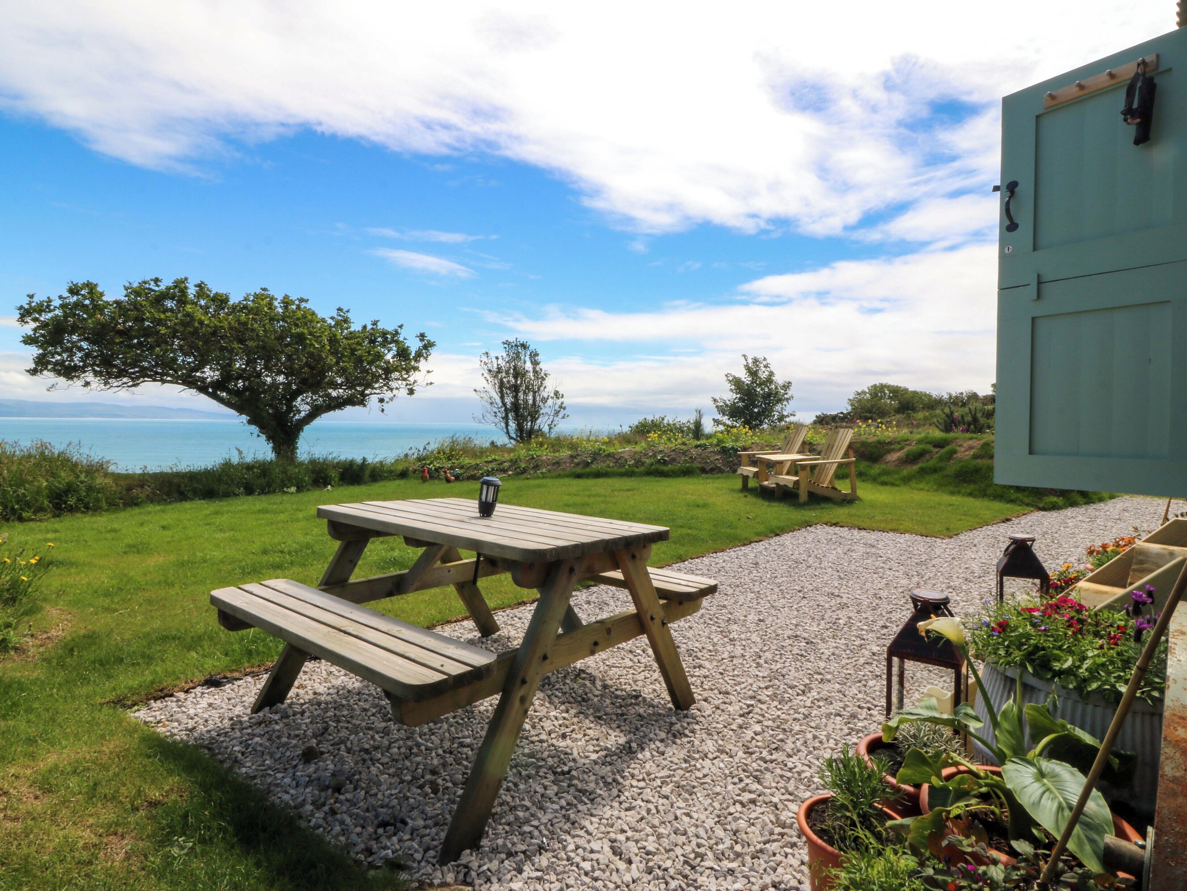 Uma mesa de piquenique e cadeiras em um jardim com vista para o mar.