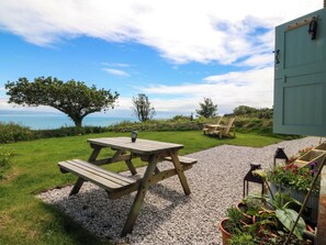 Uma mesa de piquenique e cadeiras em um jardim com vista para o mar.