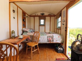 Quarto de cabana aconchegante com cama, cadeira de madeira, mesa e vista para o exterior.