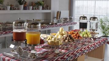 Disposição de buffet com estação de café, frutas e toalha de mesa estampada.