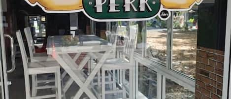 Uma janela de vidro com uma placa que diz 'CENTRAL PERK' e cadeiras brancas dispostas do lado de fora.