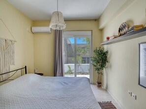Quarto com cama, um painel de macramé na parede, planta em vaso e janela com vista.
