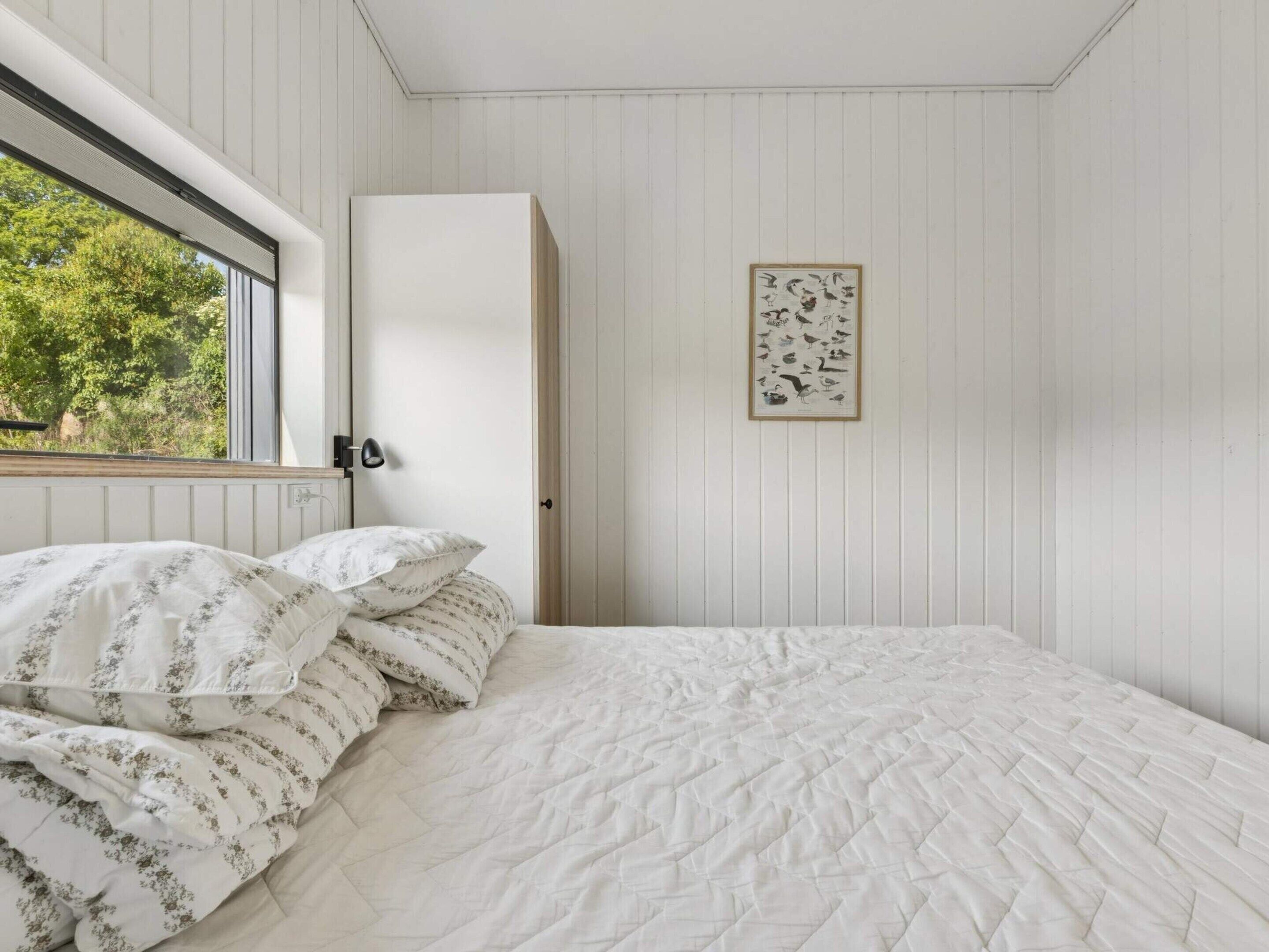 Um quarto com cama, janela, radiador, guarda-roupa e um quadro na parede.