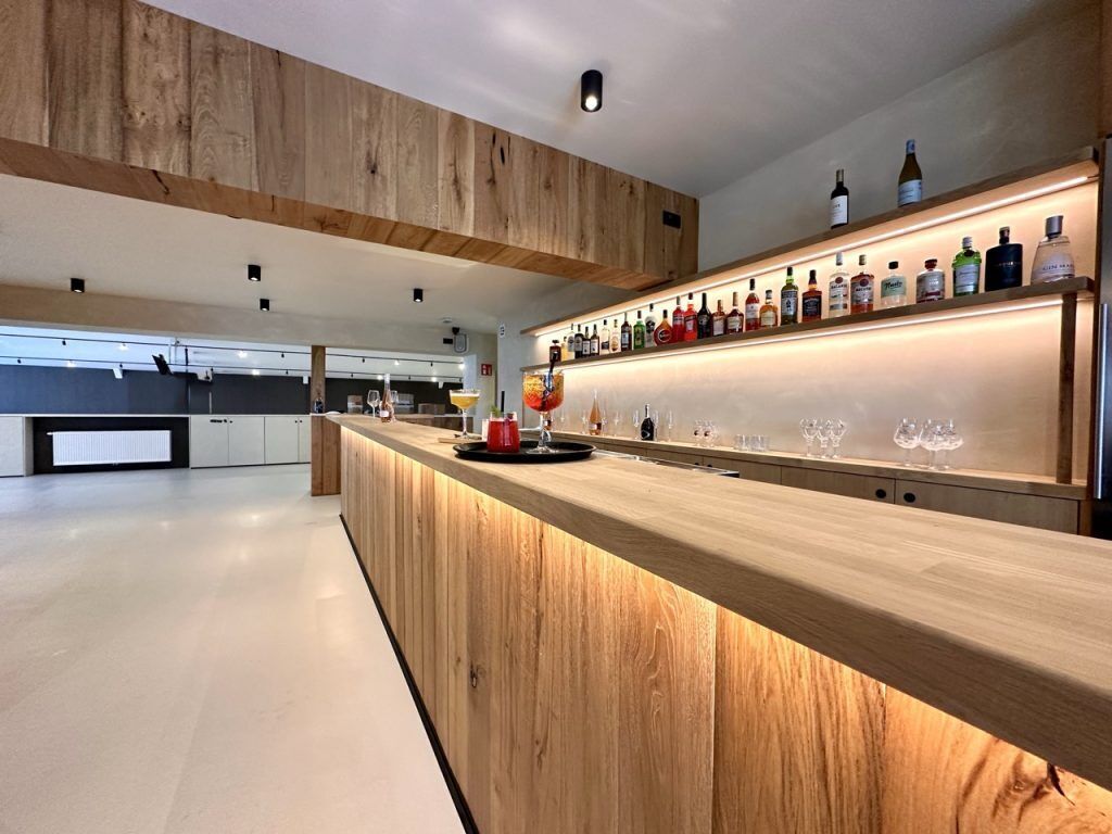 Uma área de bar moderna com detalhes em madeira, variedade de garrafas de bebidas e um design limpo e minimalista.