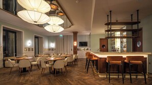 Um restaurante com piso de madeira, diversas mesas de jantar, cadeiras e luminárias pendentes.