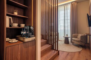 Uma sala de estar moderna com escada de madeira, máquina de café e poltrona estampada.