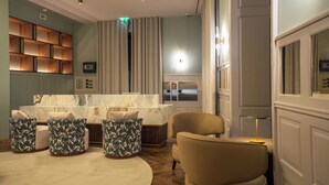 Quarto de hotel com toucador de mármore, estante de madeira, tapete redondo e poltrona bege.