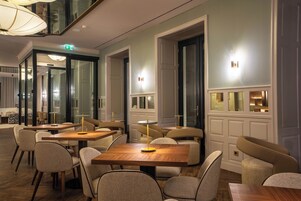 Um hall de hotel moderno com mesas e cadeiras de madeira, um painel de vidro e uma escada.