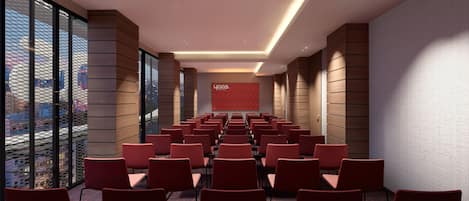 Sala de conferência com fileiras de cadeiras, uma tela grande e vista da cidade através de amplas janelas.