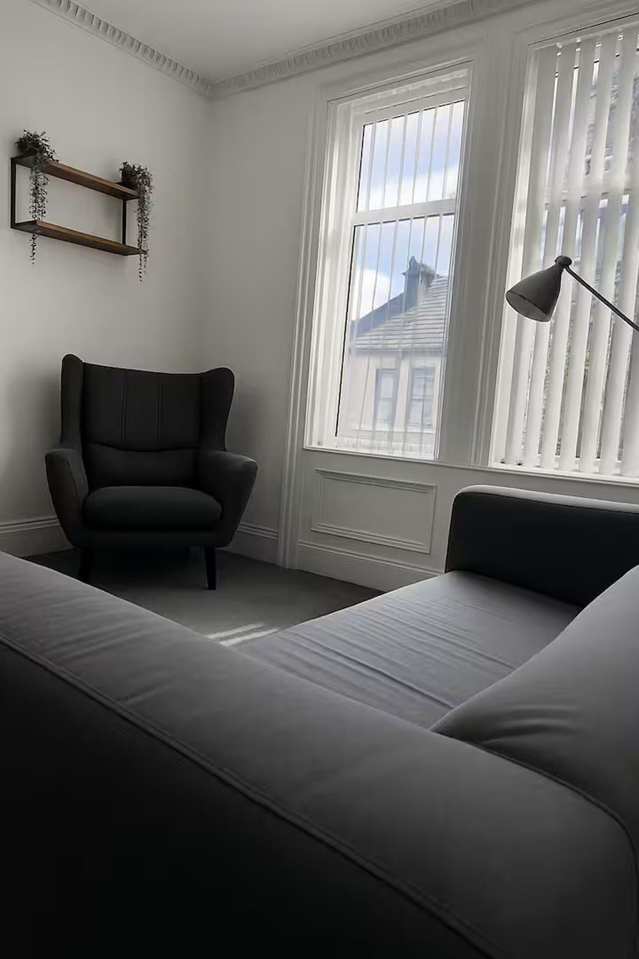 Um quarto com sofá, uma poltrona, janela com persianas e luminária de chão.