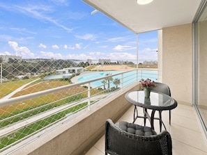 Uma varanda com vista para uma piscina, área gramada e edifícios ao longe.