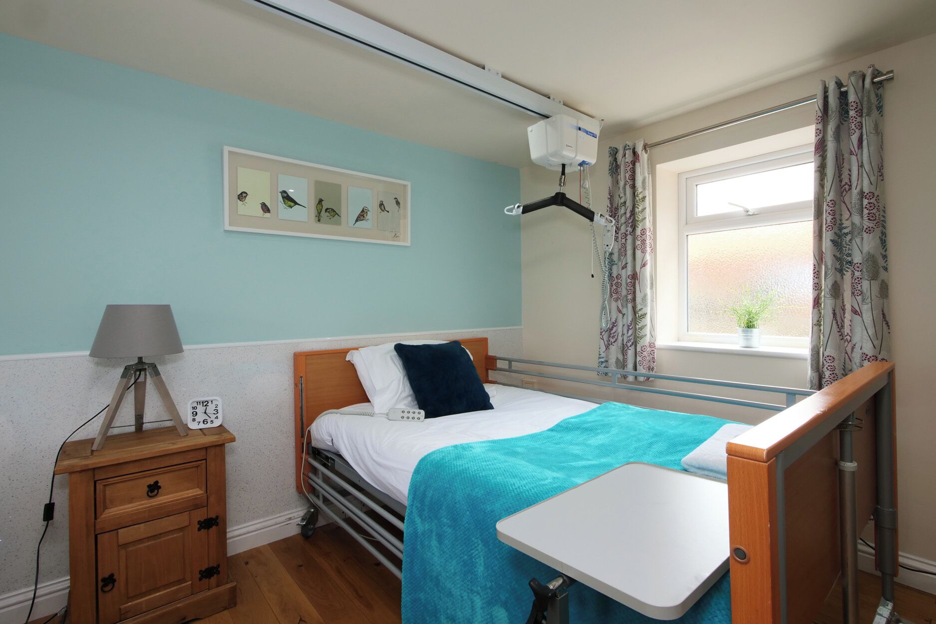 Um quarto de hospital com uma cama, uma mesa de cabeceira com abajur, uma janela com cortinas e um relógio na parede.