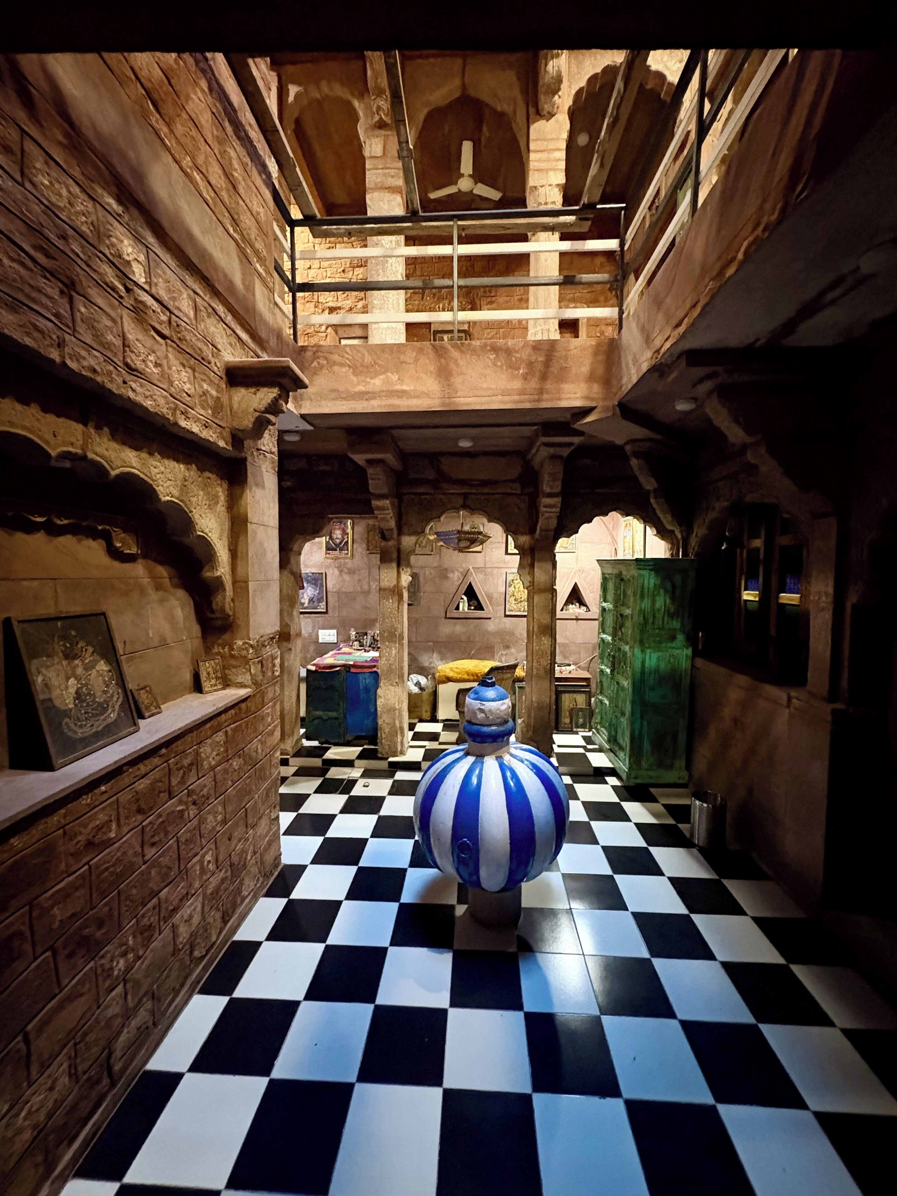 Um interior com piso xadrez, um objeto esférico azul e branco decorativo e paredes de pedra.